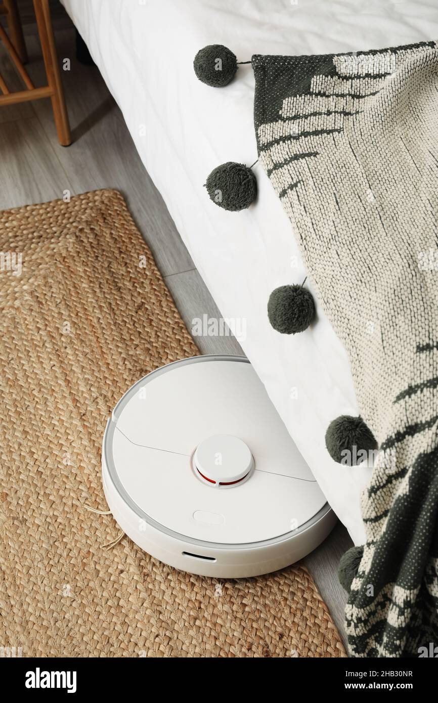 Modern robot vacuum cleaner near bed in room Stock Photo - Alamy