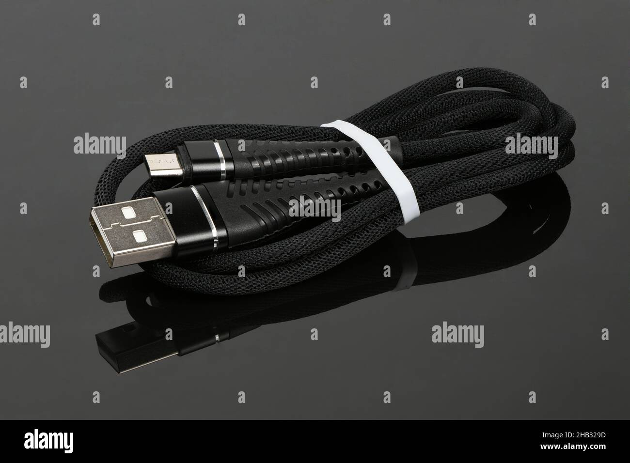 Black USB cable for charging a smartphone on black acrylic background ...