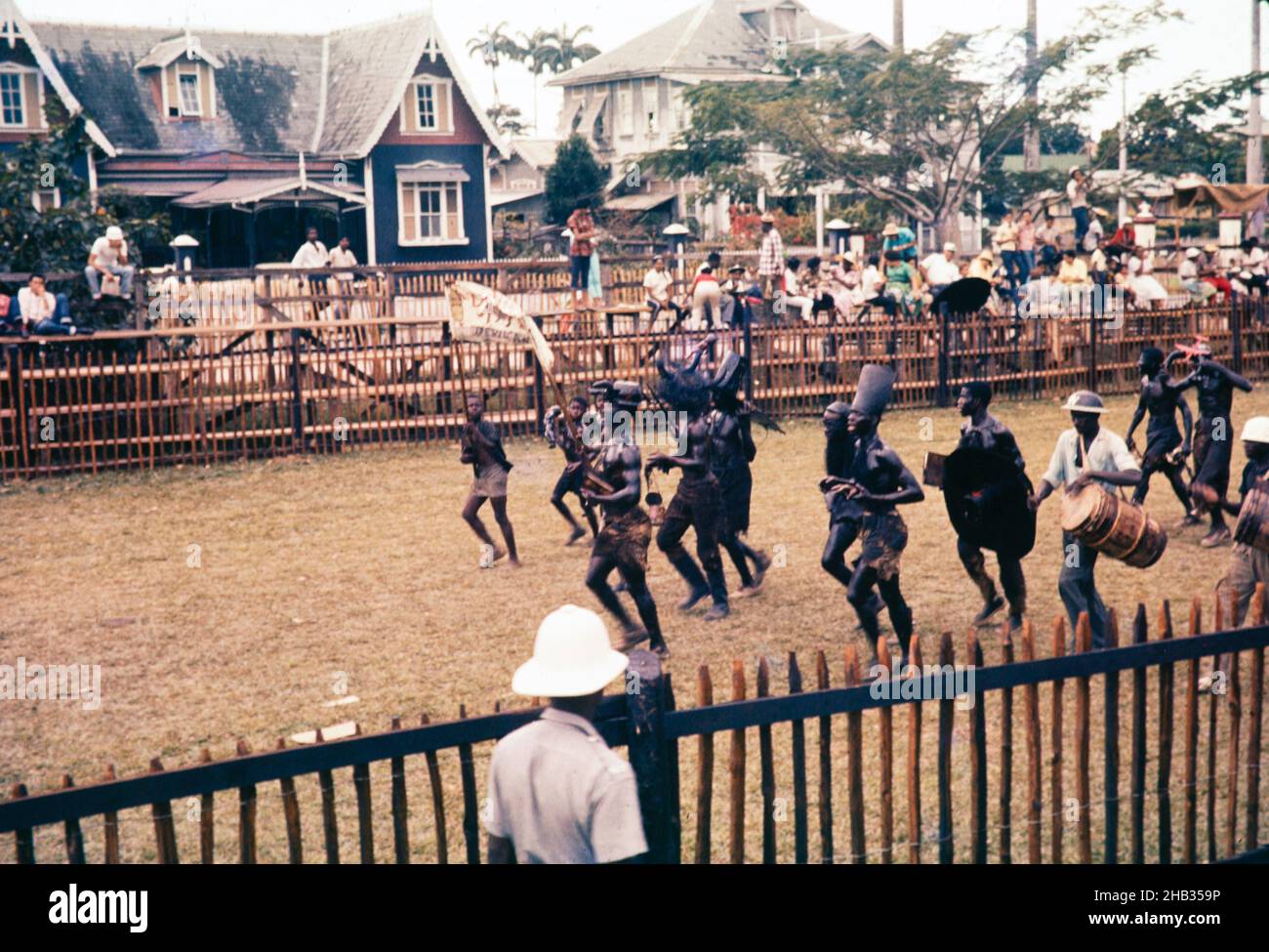 Carnival group in black tar costumes watched by policeman with white ...