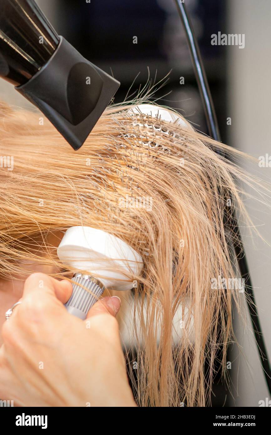 Hairdresser hand drying blond hair with a hairdryer and round brush in ...