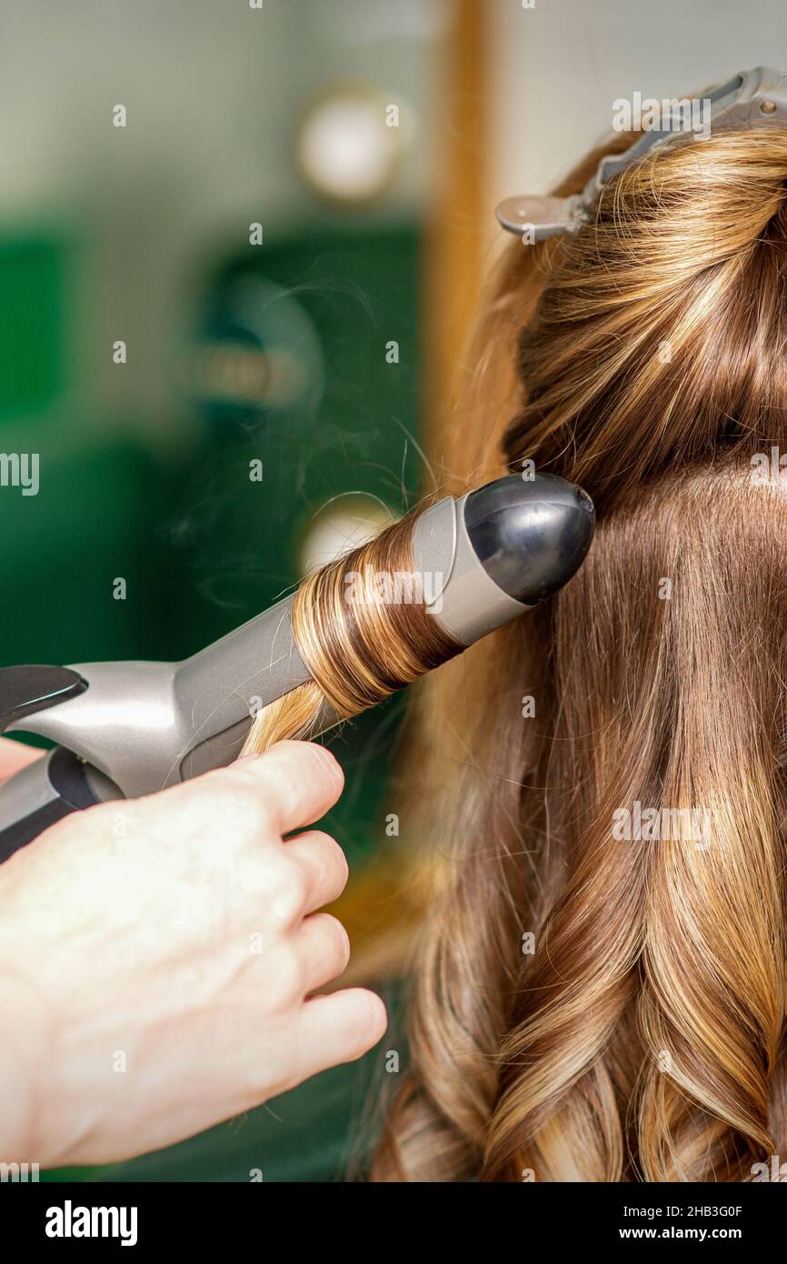 Creating curls with curling irons. Hairdresser makes a hairstyle for a ...