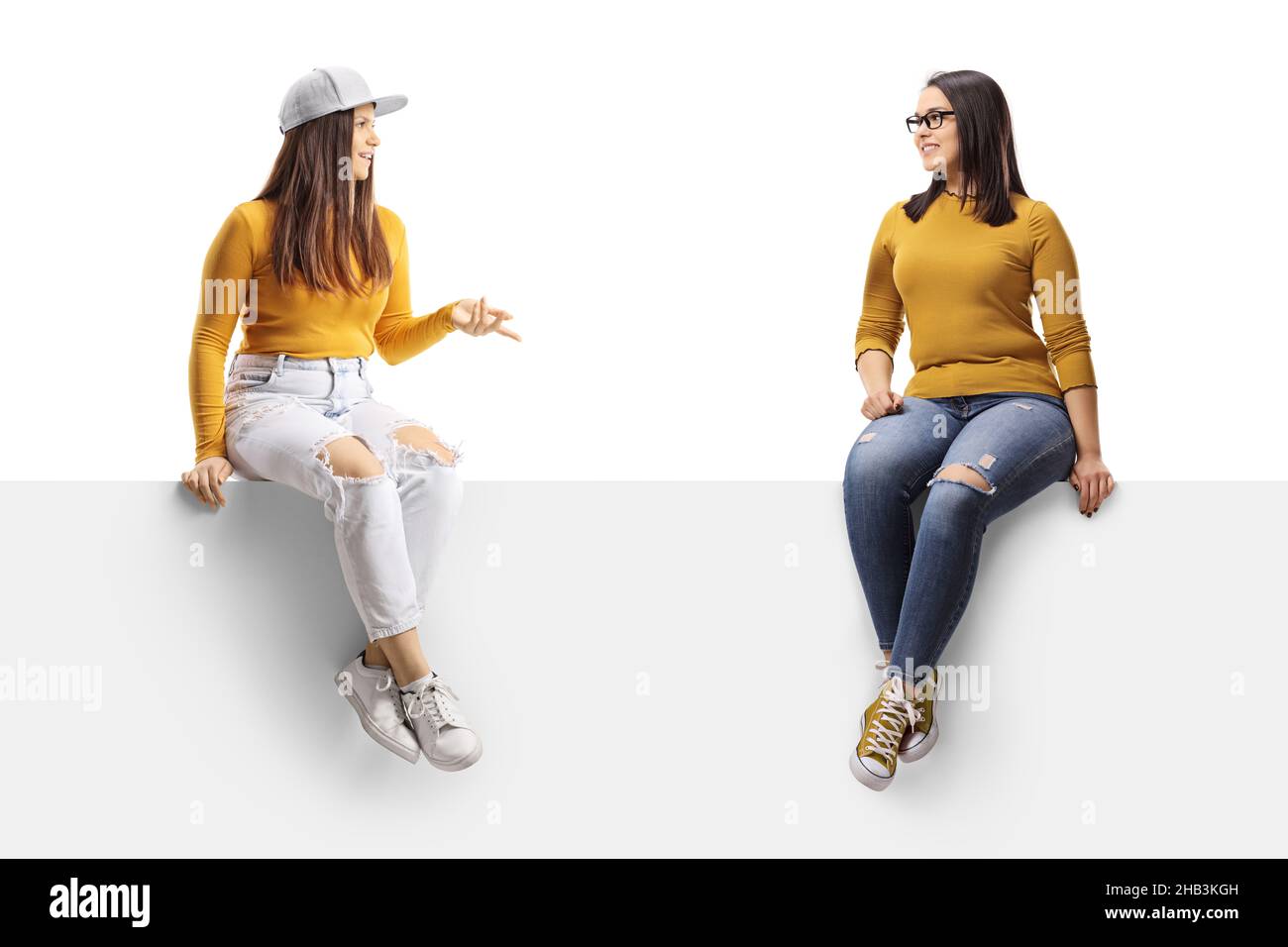 Two young female friends sitting on a blank panel and having a ...