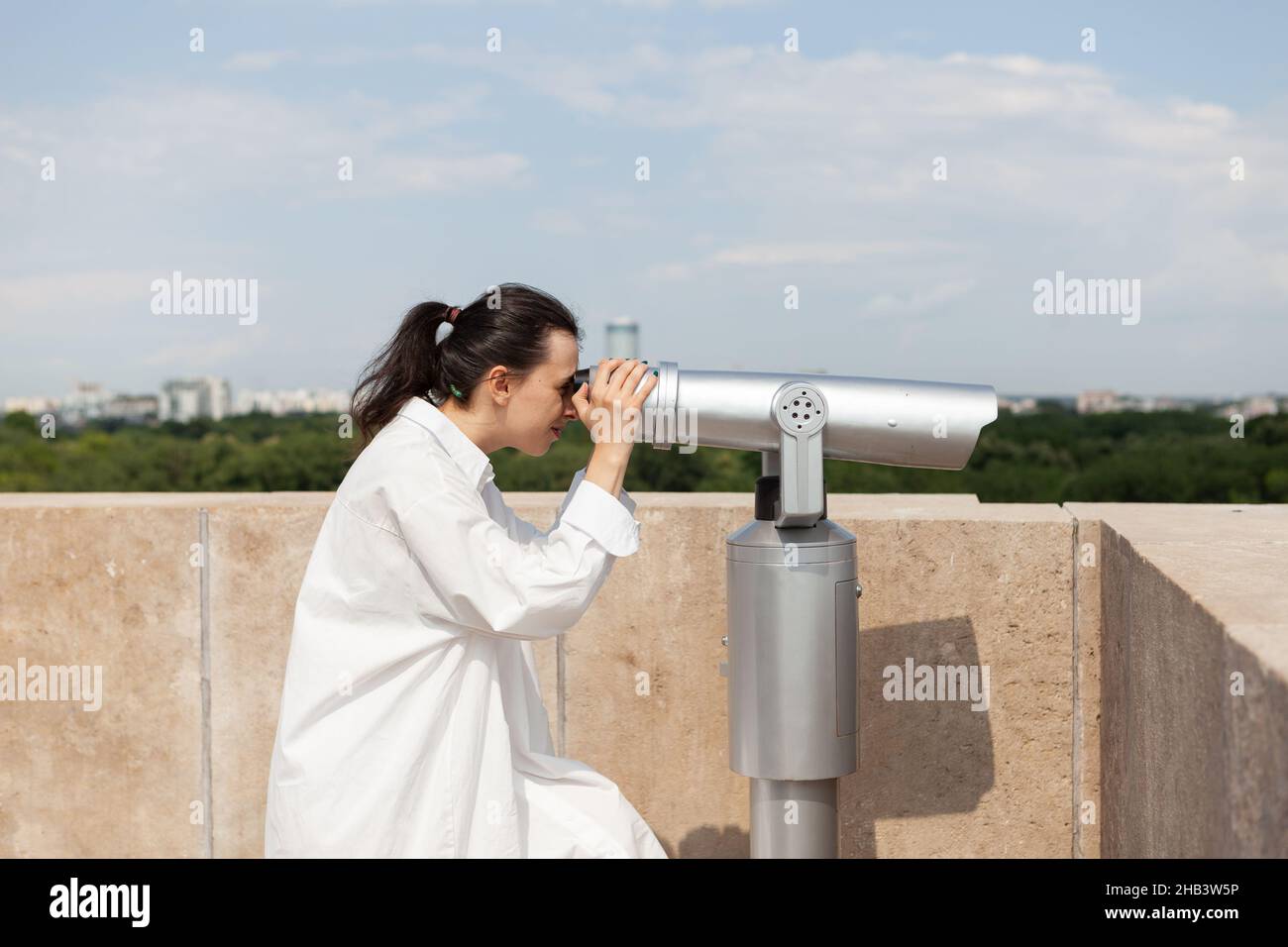 Caucasian female standing on building rooftop looking through telescope ...