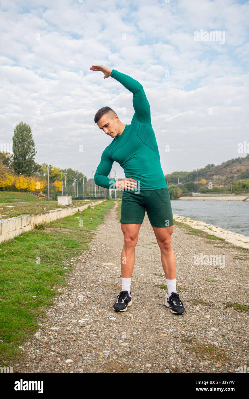 Attractive and handsome strong guy is stretching alone outside before ...