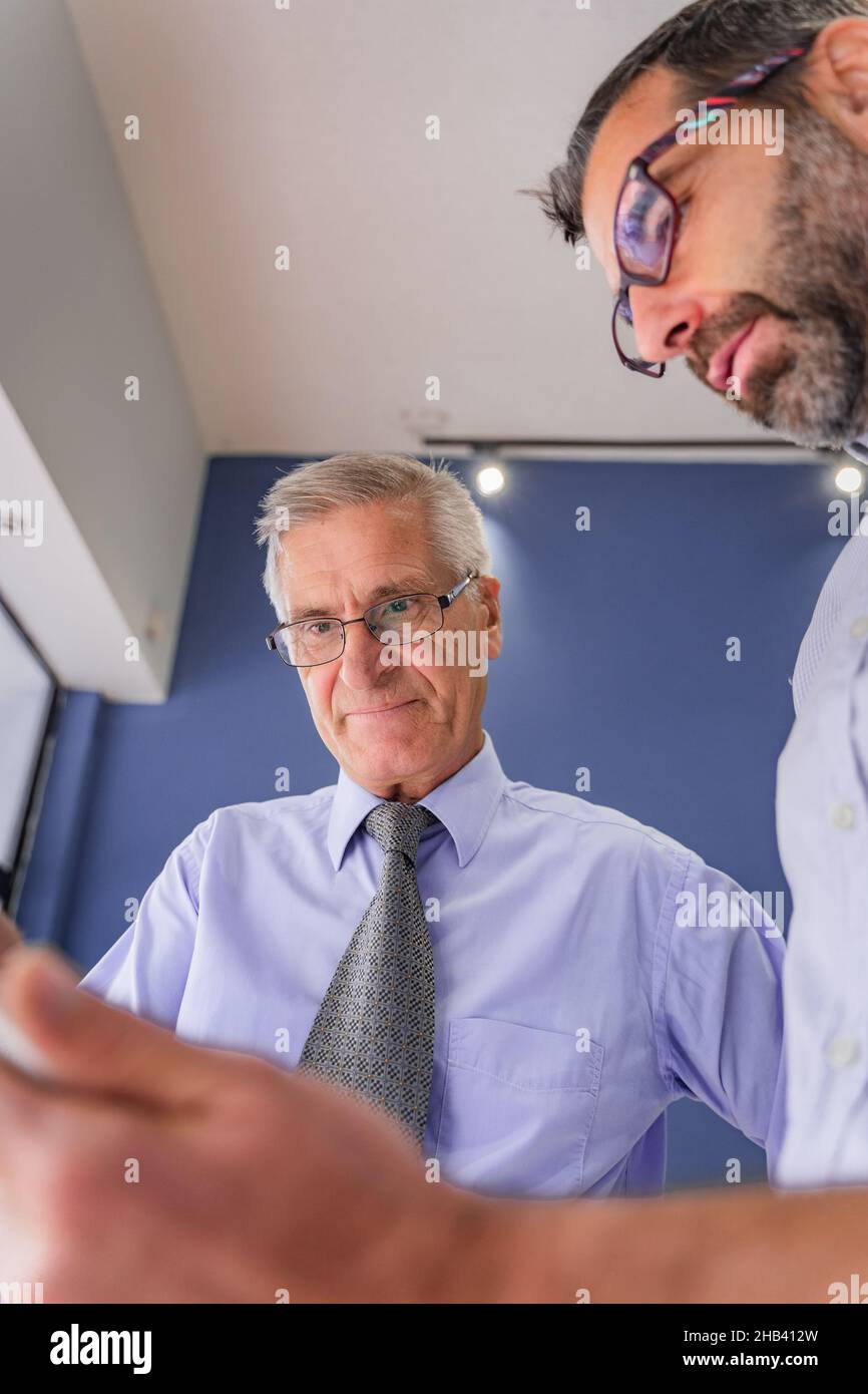 Two senior businessmen are standing and thinking while talking about ...
