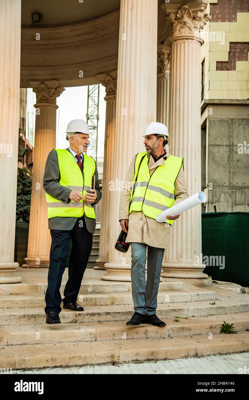 Two construction workers are walking and talking to each other about ...