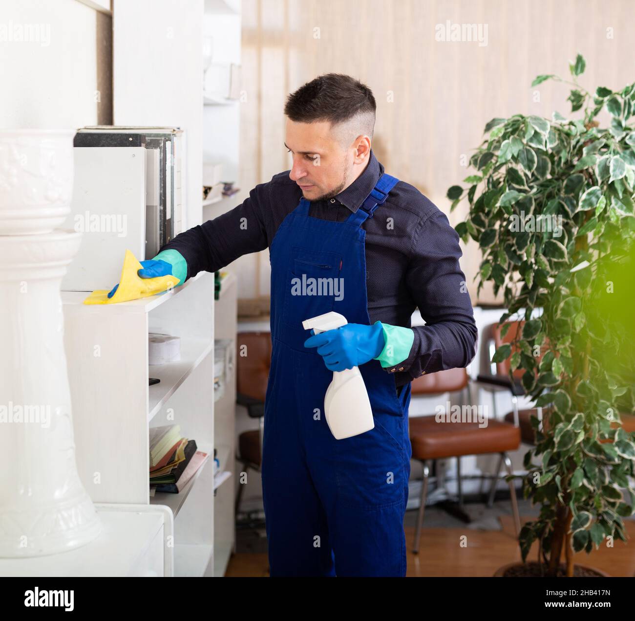 Cleaner wiping dust from racks in office Stock Photo - Alamy