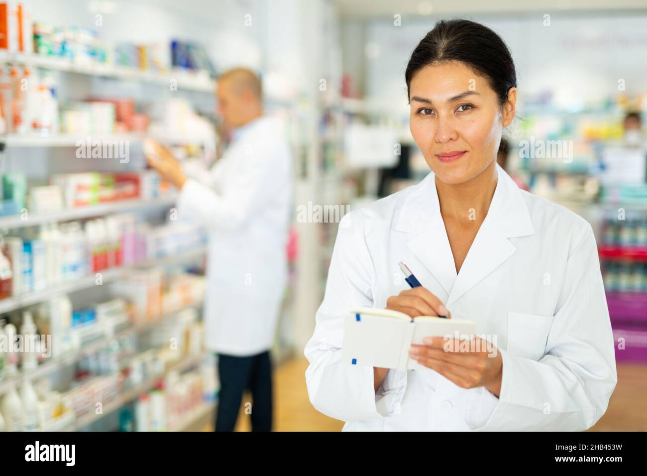 Positive female pharmacist makes notes on a notebook in the sales area ...