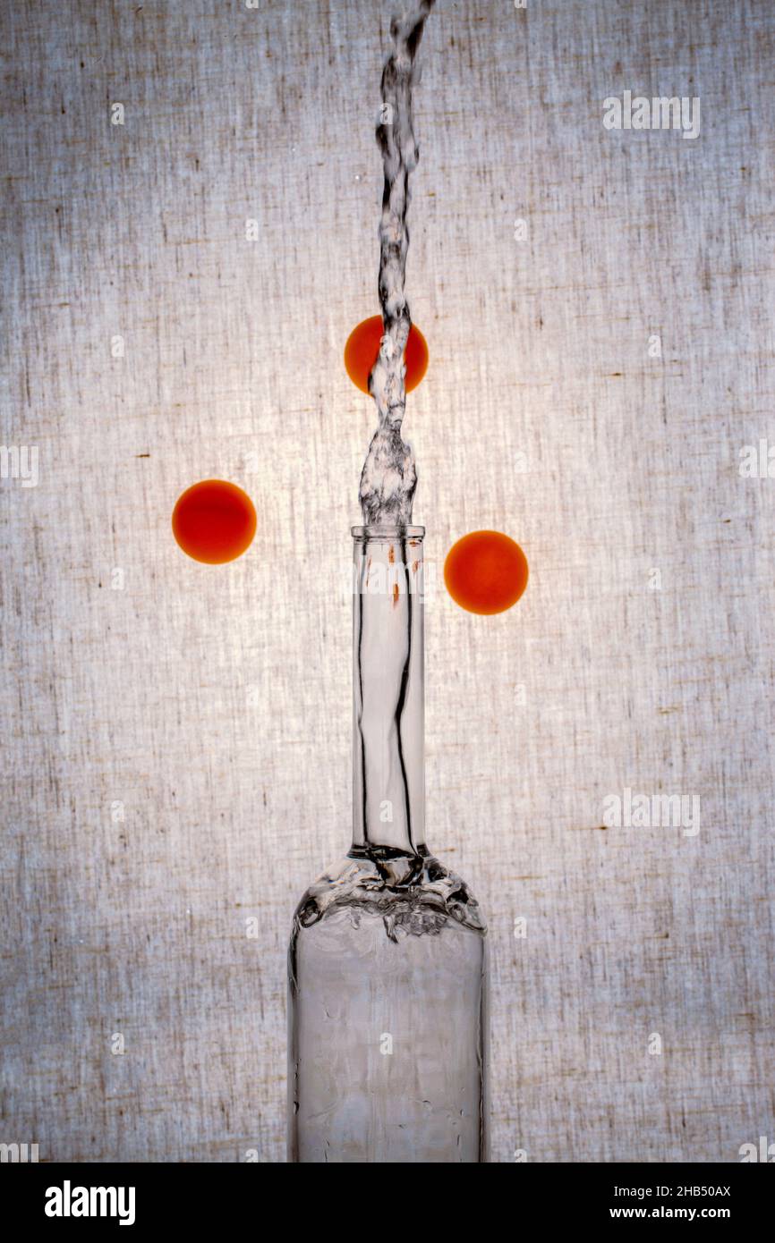 Still life with three orange balls and liquid pouring out of a glass ...