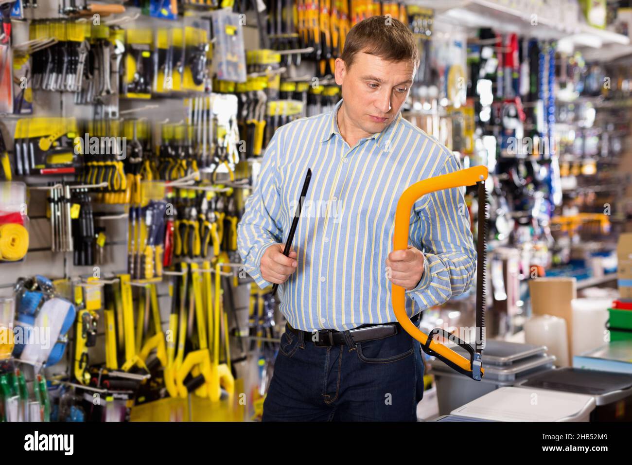 Confident man is choosing hacksaw in tools store Stock Photo - Alamy