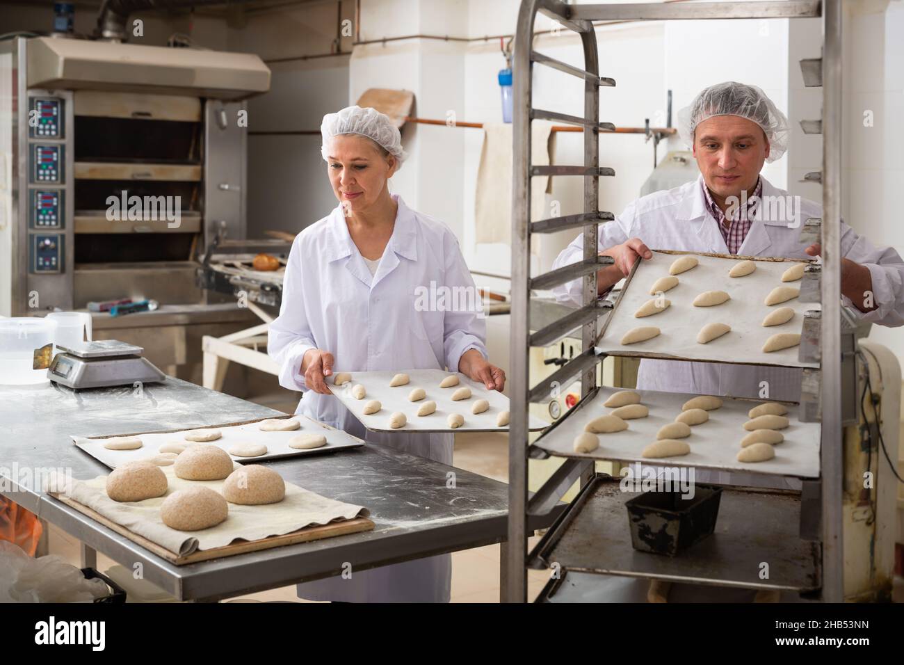 Nice baker placing tray with formed raw dough Stock Photo - Alamy