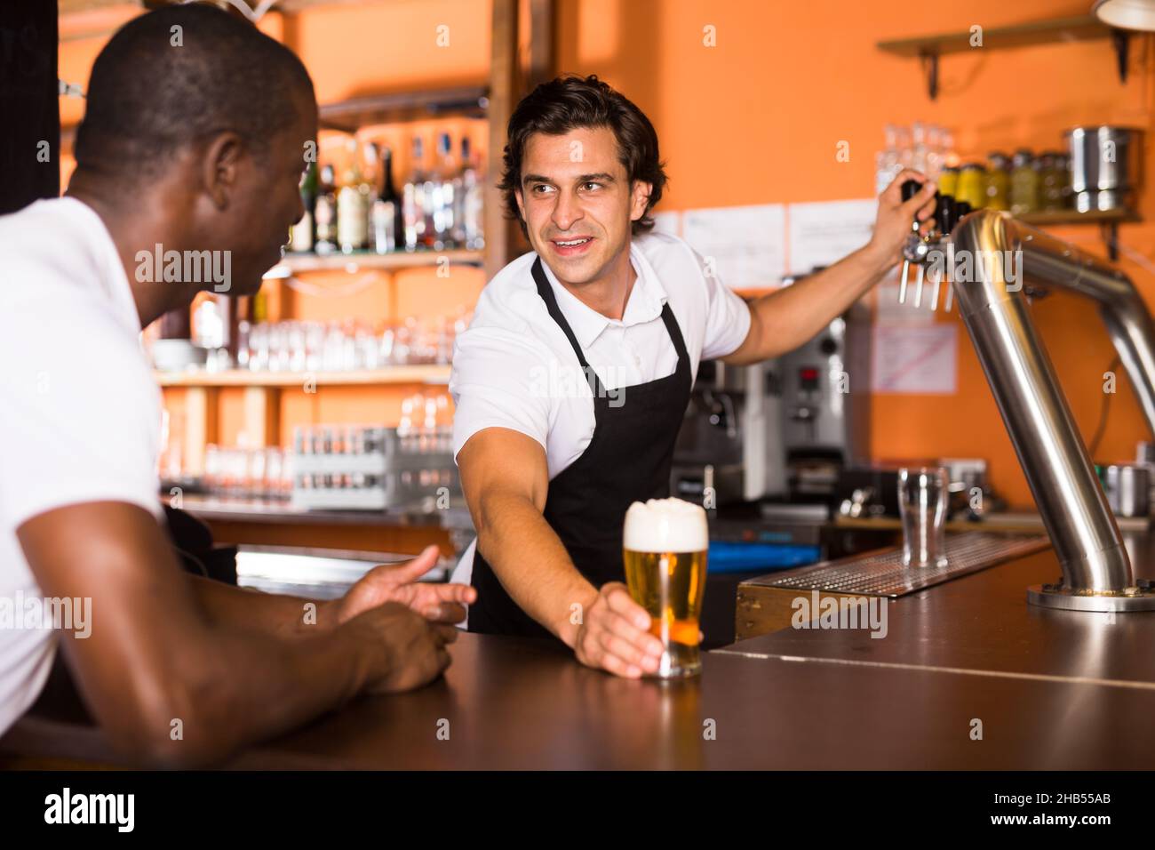 Positive man bartender giving glass of golden beer to man client Stock ...
