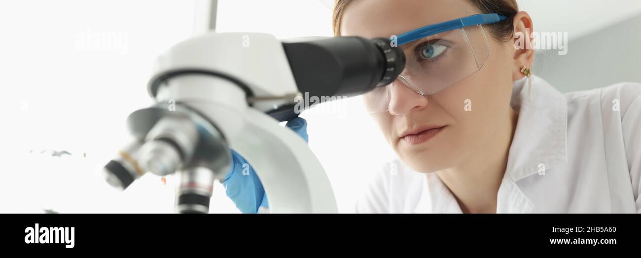Portrait of female scientist looking through microscope in laboratory ...