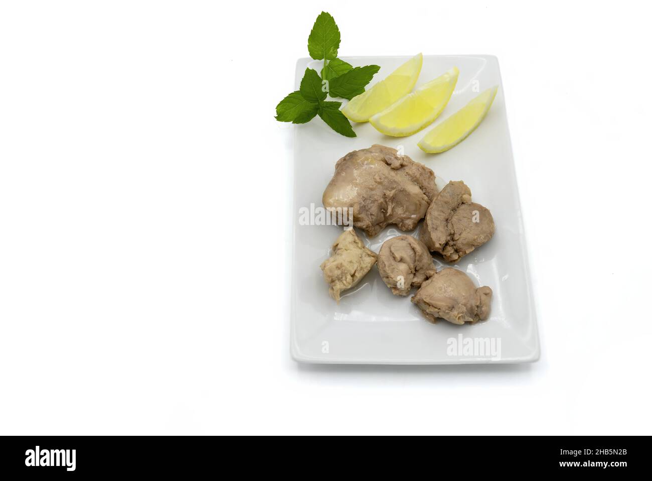 Cod liver in its oil on a plate with lemon slices and green leafs, top ...