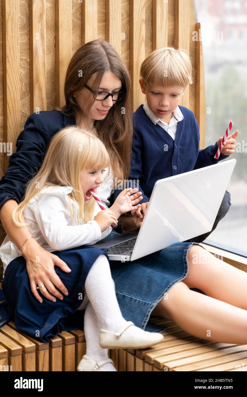 young woman working at home remotely with laptop. two children ...
