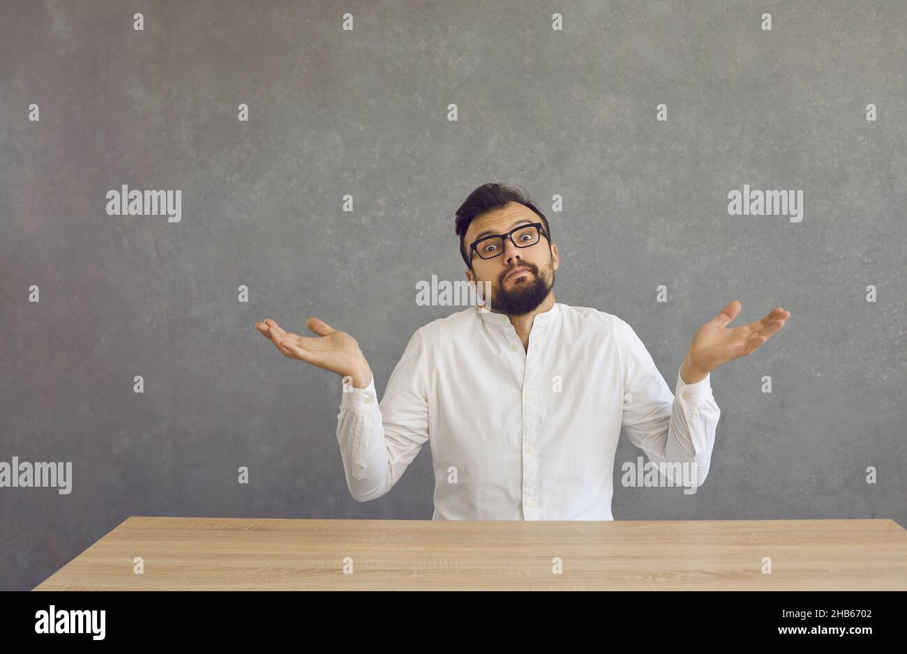 Confused young bearded man shrugs and spreads his arms with a dumb and ...