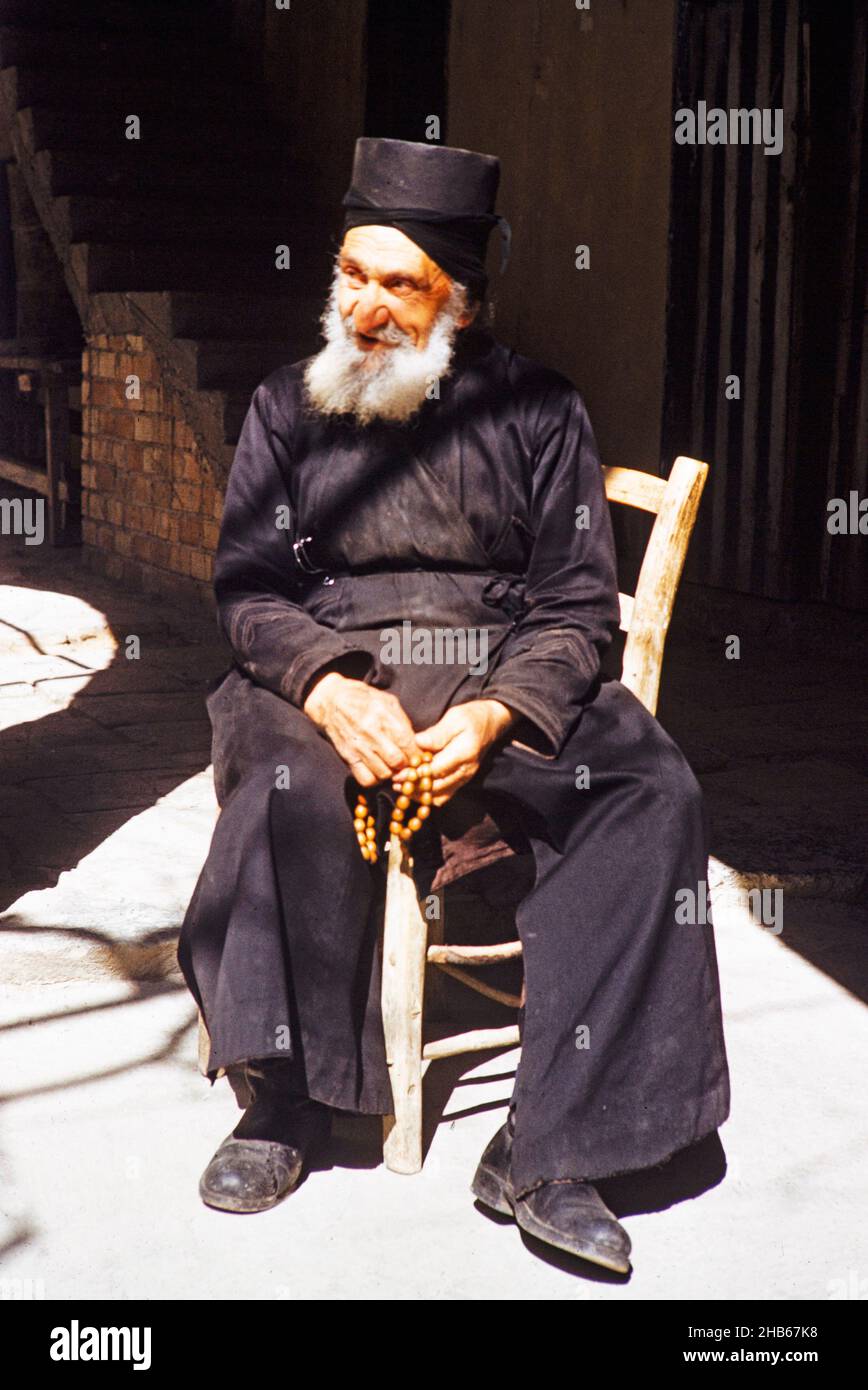 Older monk sitting outside with prayer bead, Panagia Machairas ...