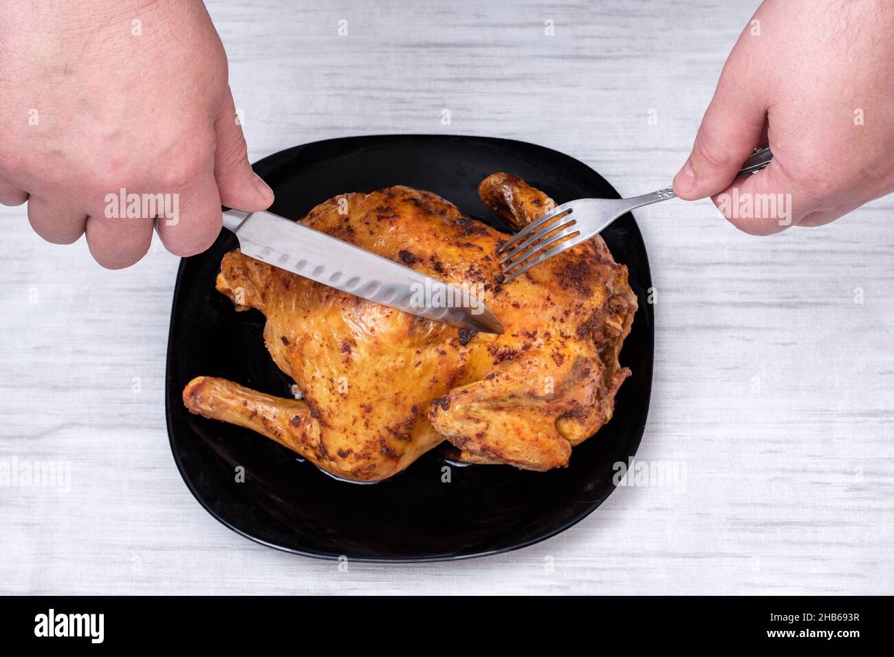 Hands holding a knife and a fork for cutting fried chicken on a black ...