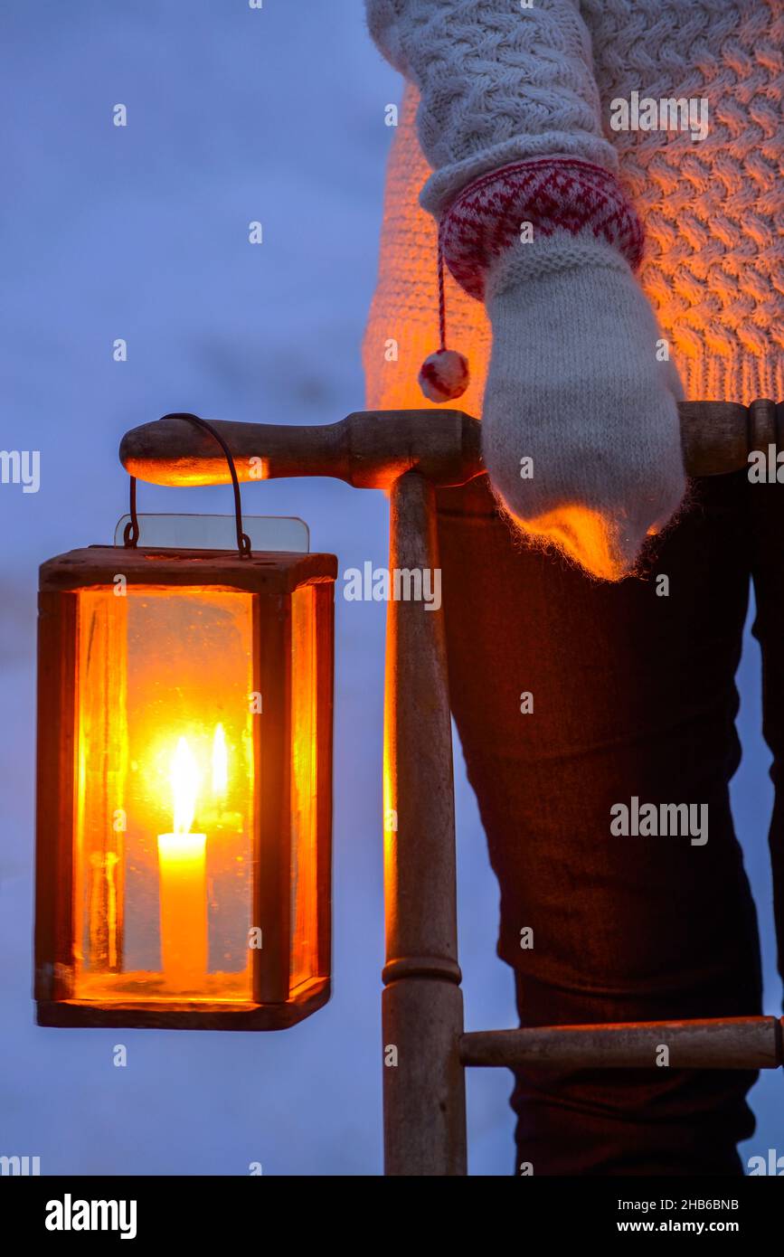 A person wearing a knitted mitten holding on a kick-sled and a lantern ...