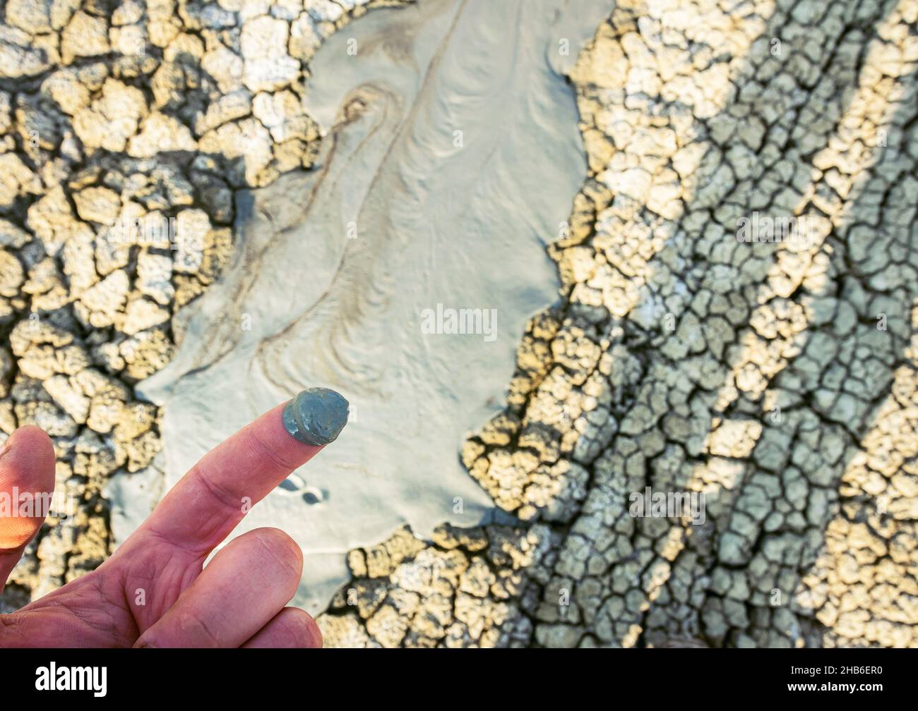Persons hand with muddy finger next to mud volcanoe in the background ...