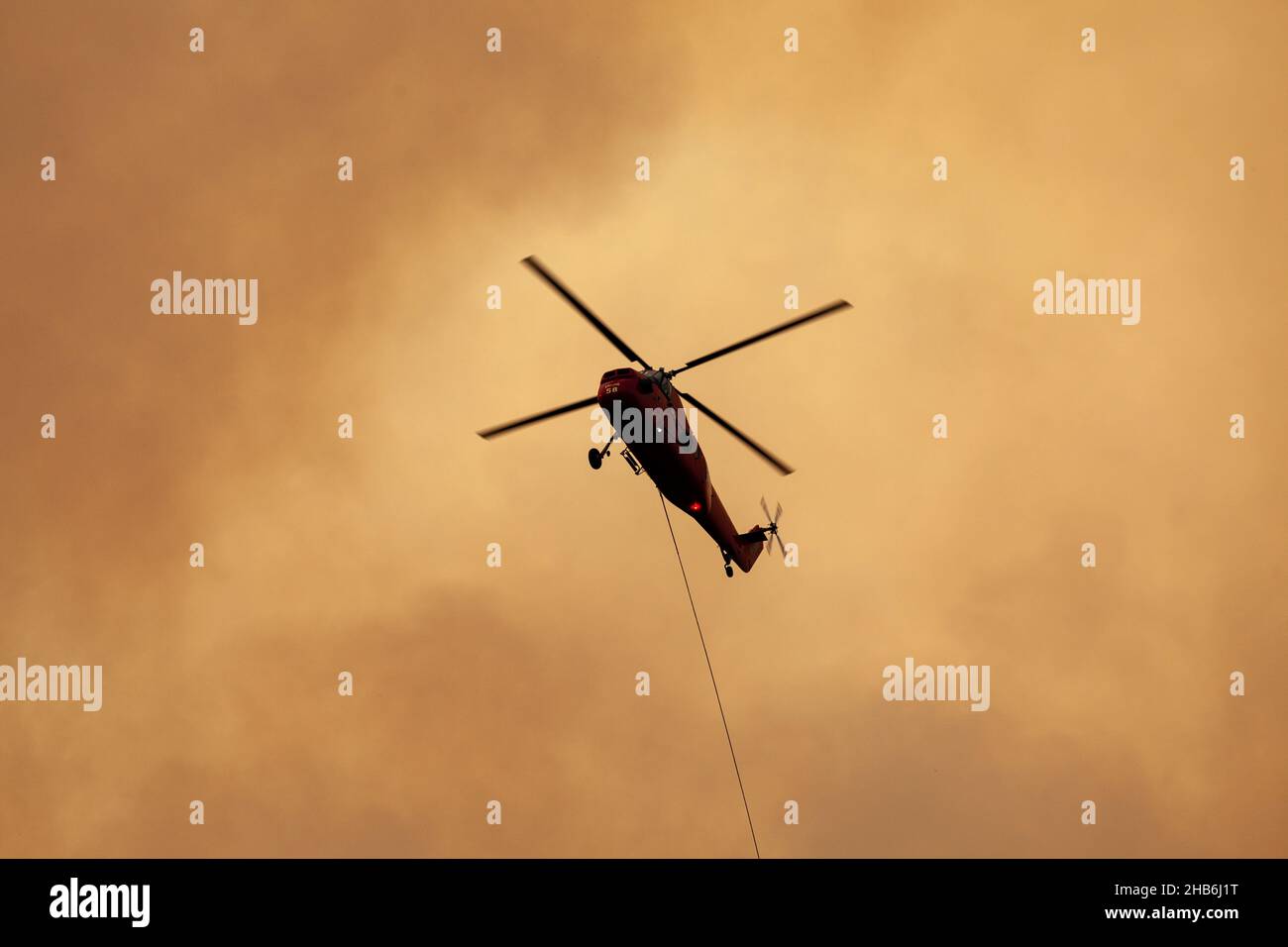 Breathtaking shot of a helicopter flying over a burning forest trying ...