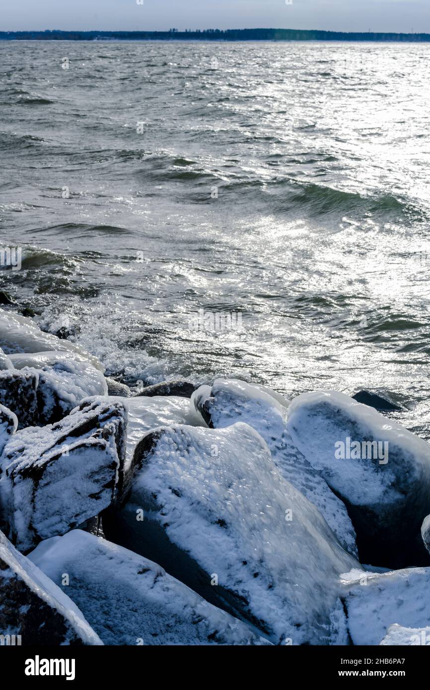 Boulders covered with ice on the shore of an unfrozen lake with waves ...