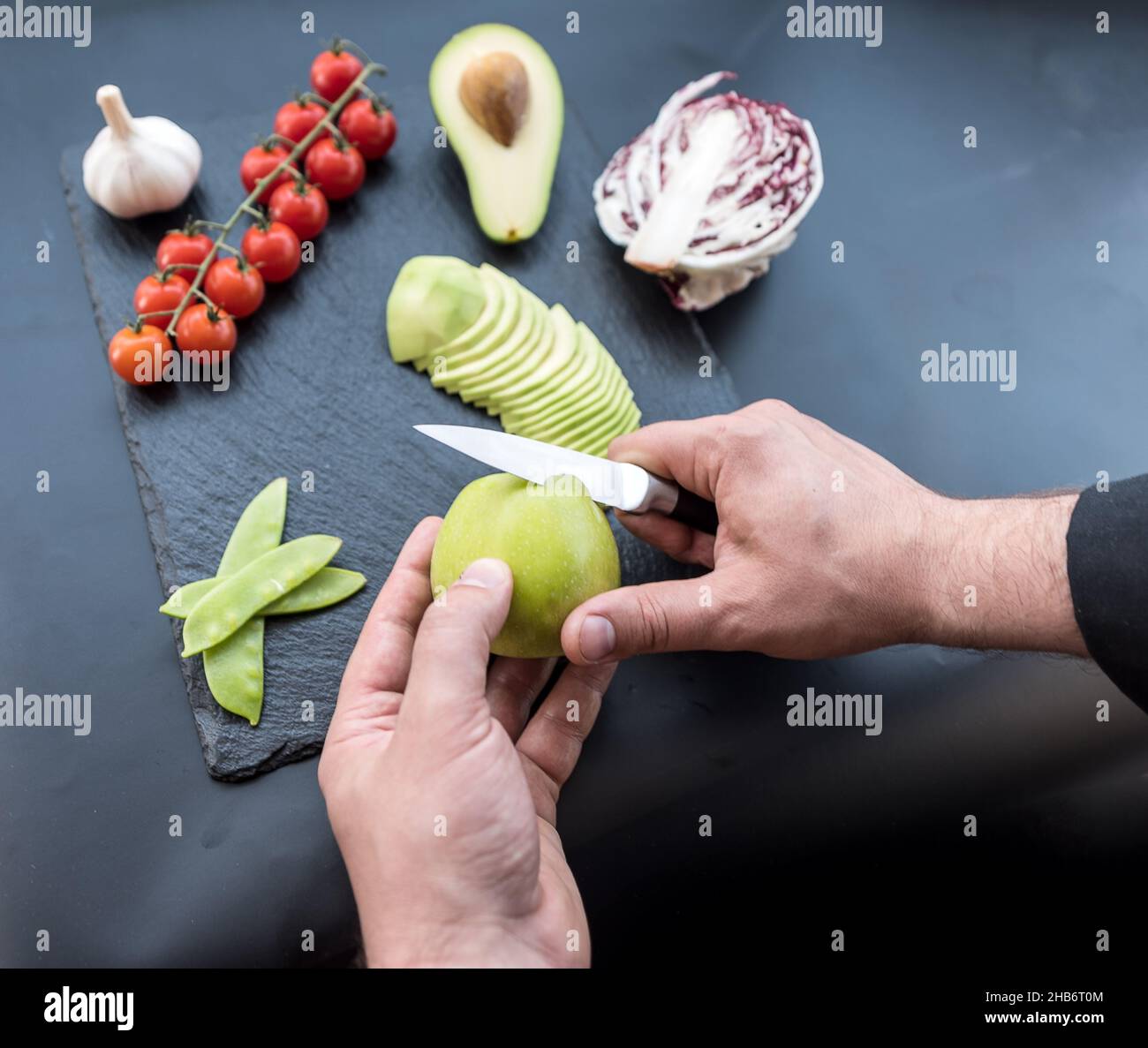 Hand with knife cutting out an apple core on a dark chopping board ...