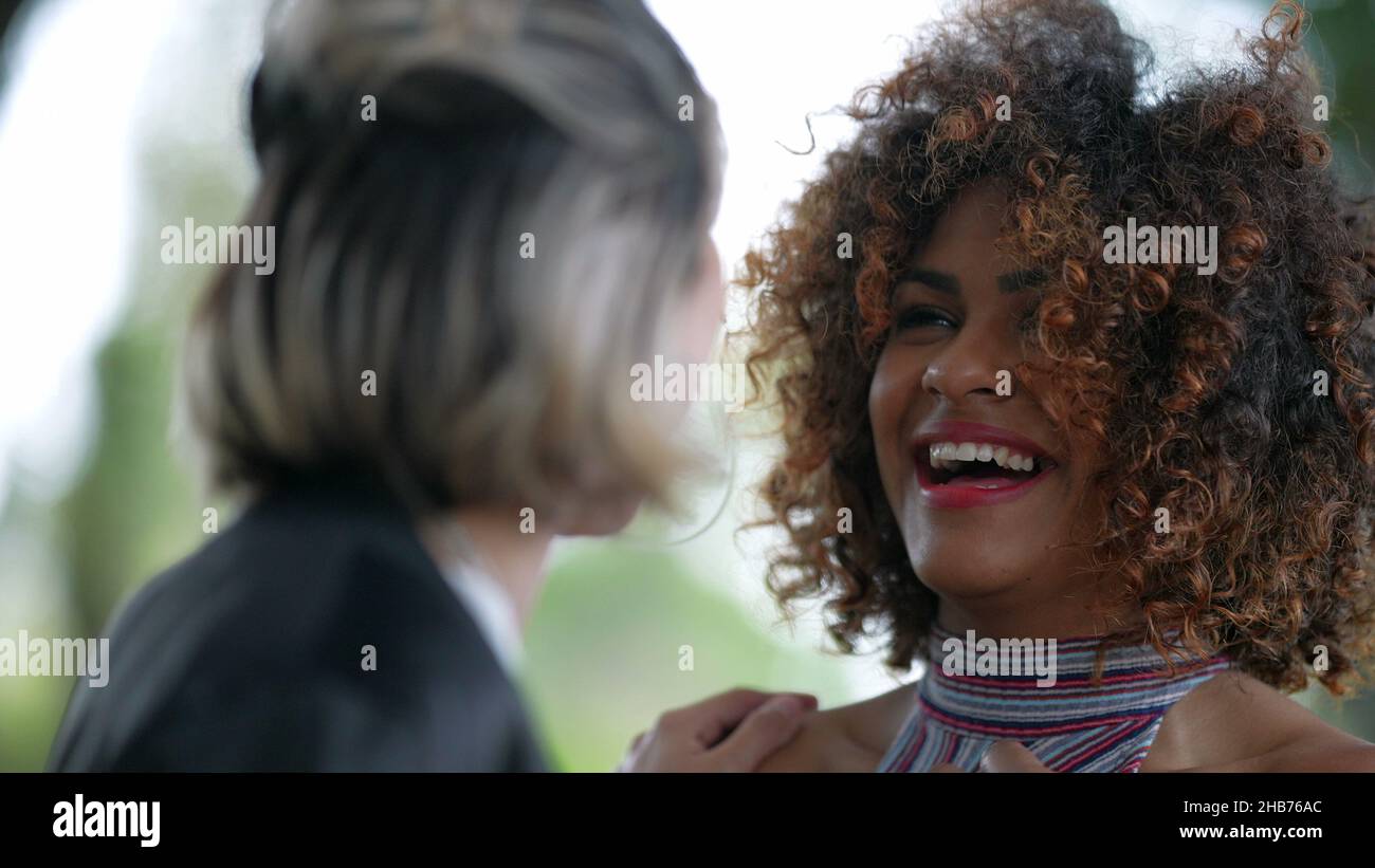 Two friends in conversation laughing and smiling, diverse latina ...