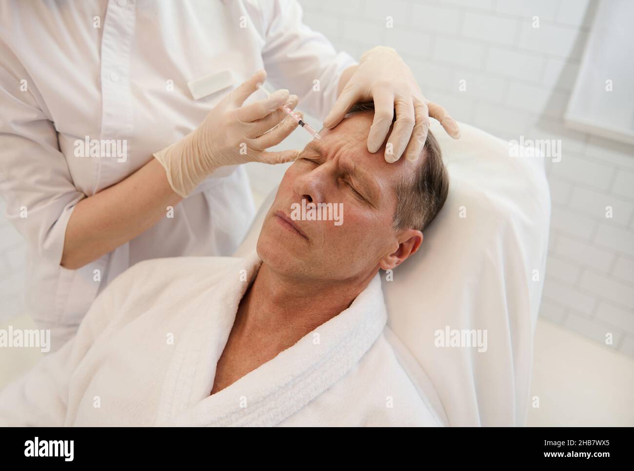 Men's cosmetology. Beautician injects a botulinum toxin into a man's ...