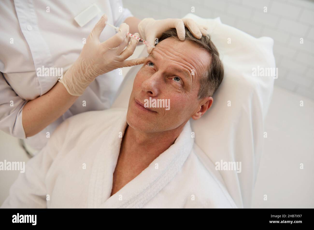 Men's cosmetology. Beautician injects a botulinum toxin into a man's ...