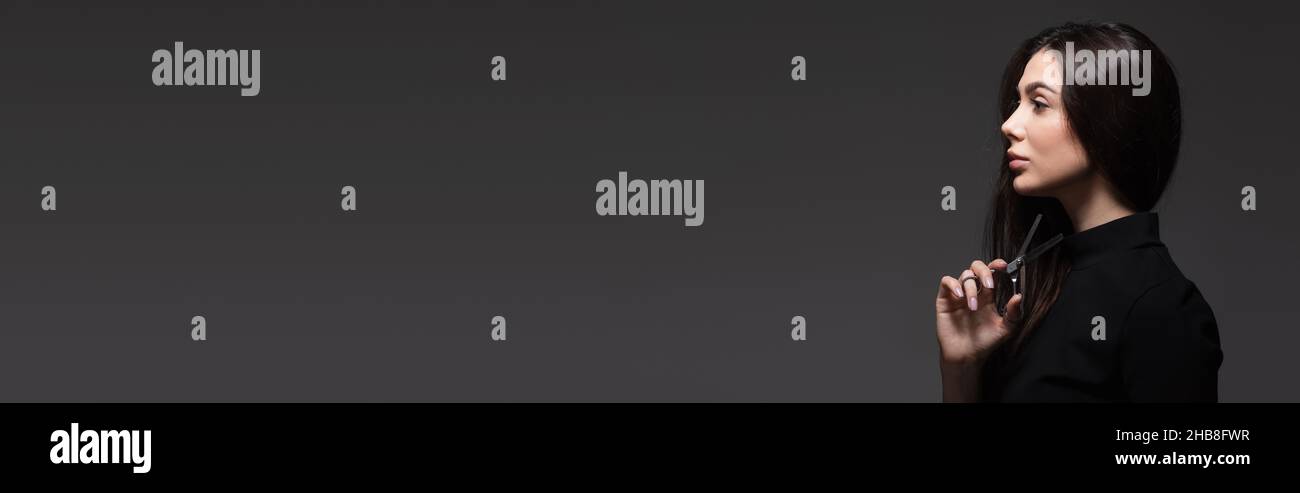 side view of woman holding scissors near long shiny hair isolated on ...