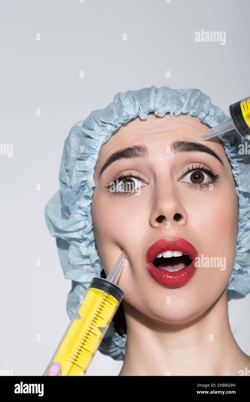 huge syringes near face of shocked young woman in surgical cap isolated ...