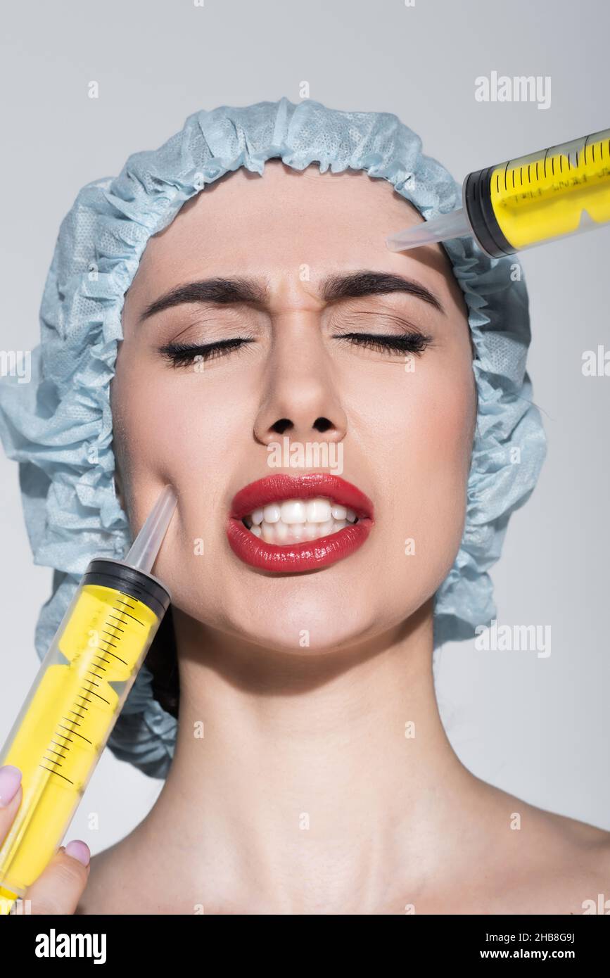 huge syringes near face of scared young woman in surgical cap isolated ...