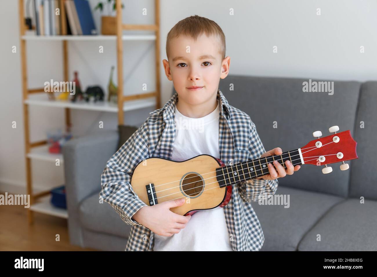 Talented kid holding soprano ukulele at home. Preschool boy learning ...