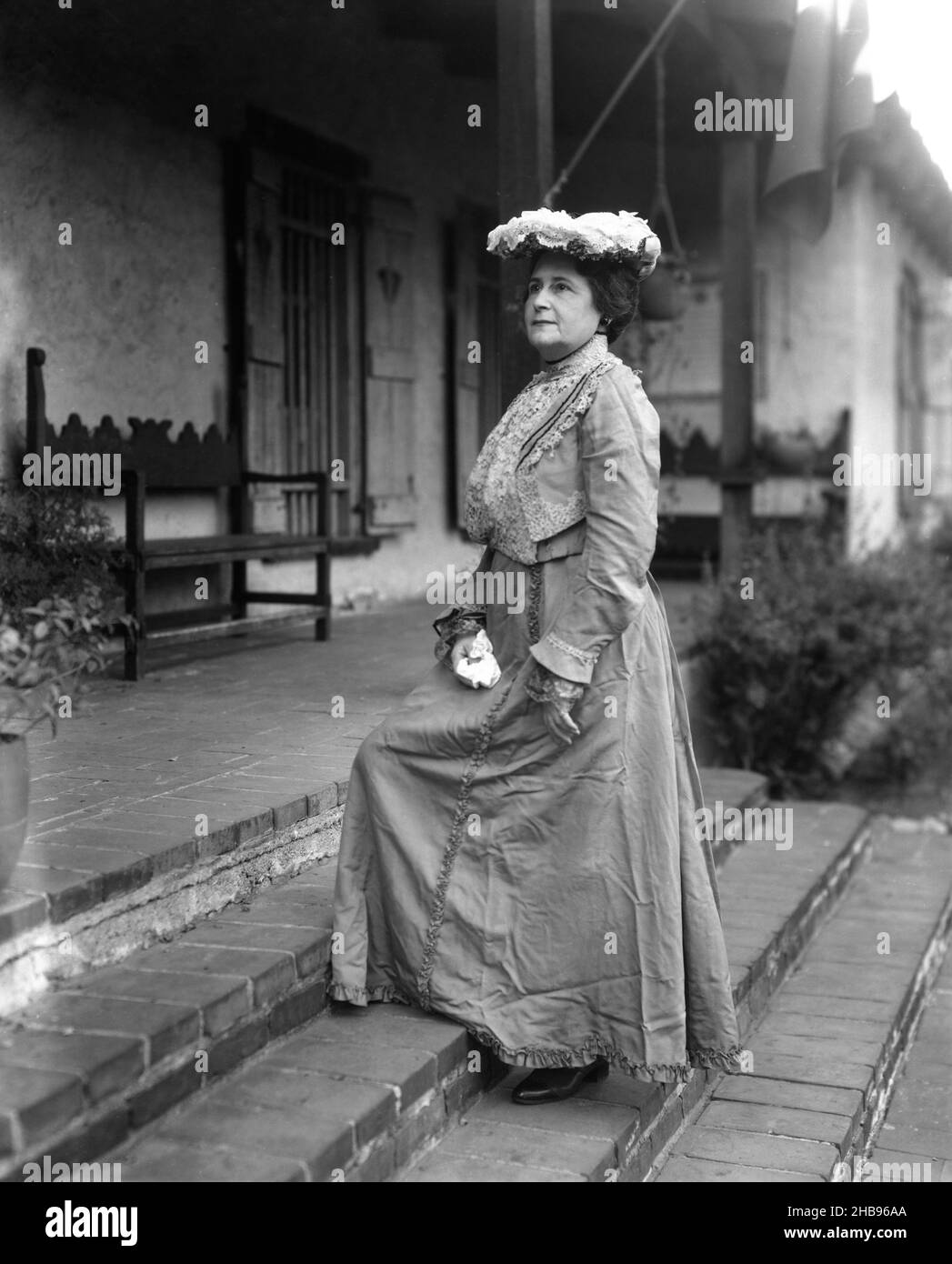 Older woman posing in historic dress with hat walking up brick steps ...