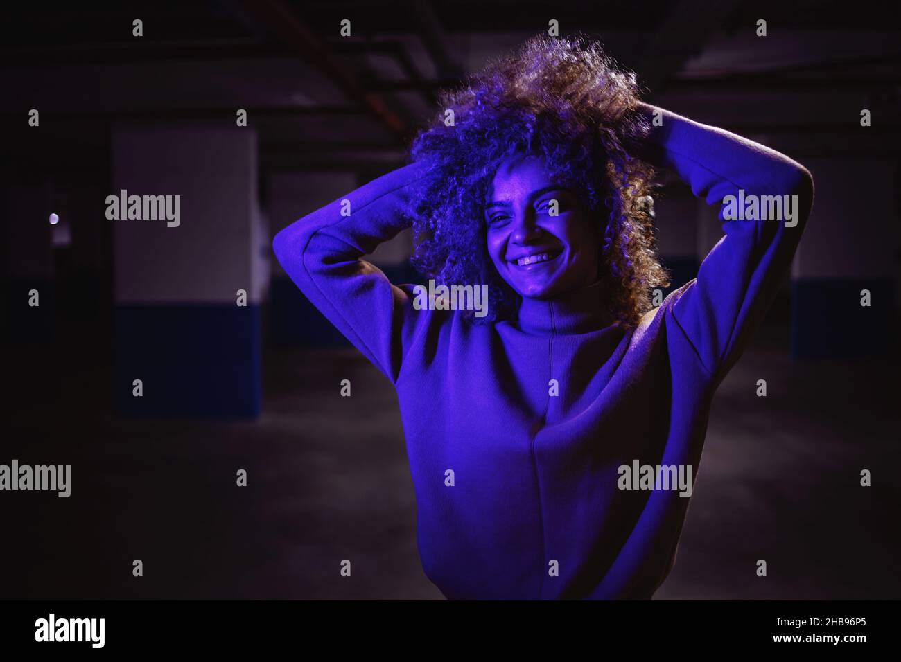 Smiling rap girl posing in underground garage under purple lights and ...