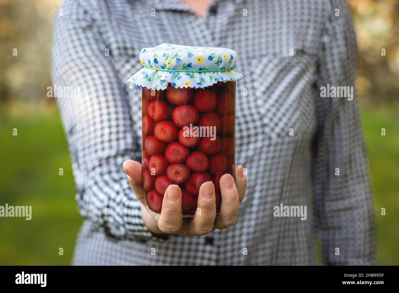 Woman holding red cherry compote outdoors. Homemade preserved fruit in ...