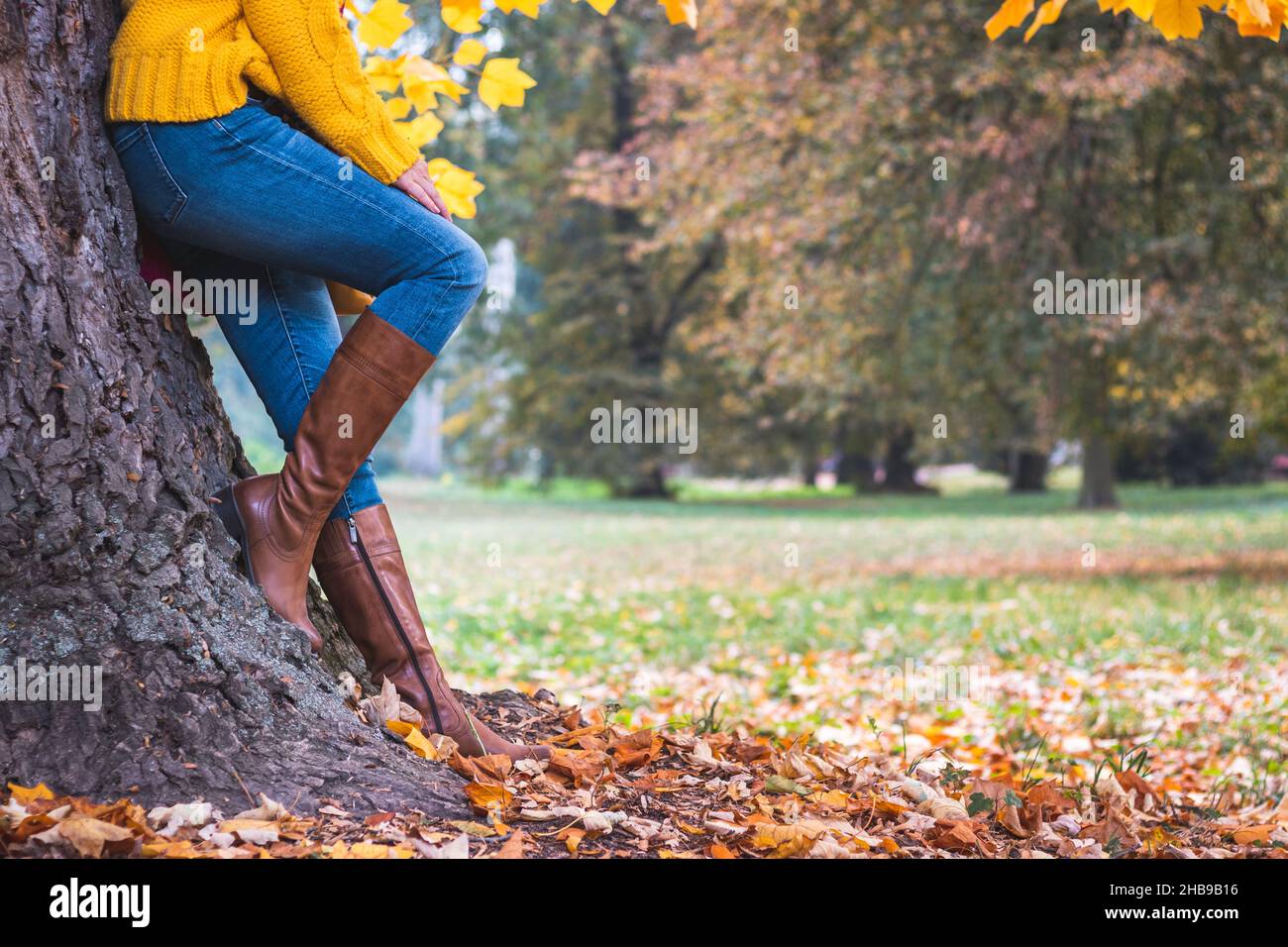 Fashion woman is leaning on tree at autumn park. Female legs wearing ...