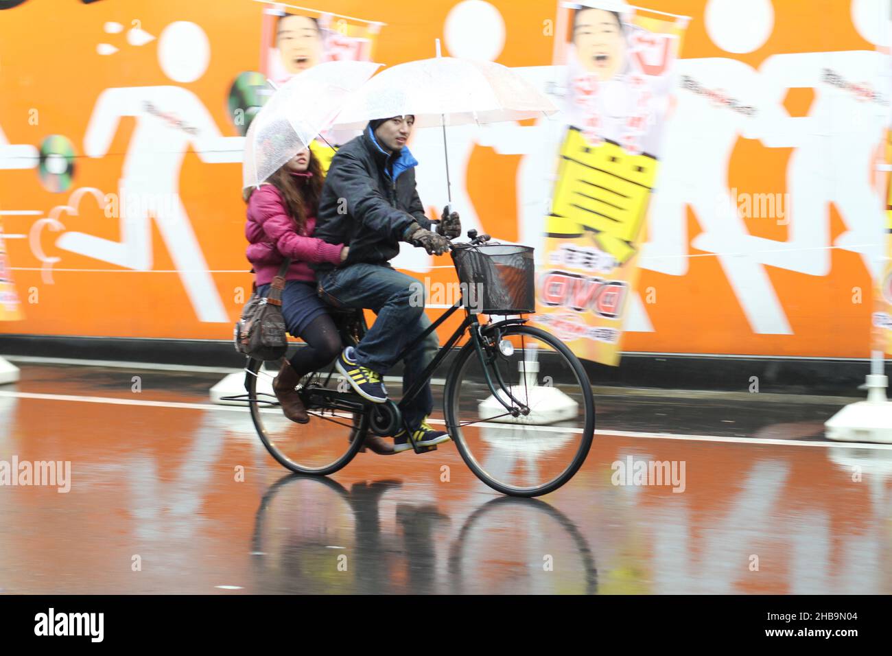 People biking in the rain with an umbrella in the streets in Osaka ...