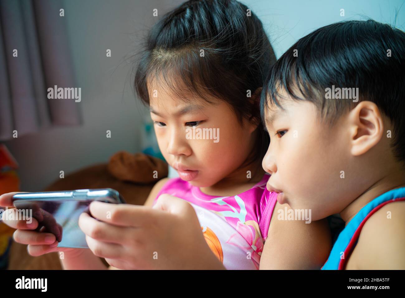 Brother and sister two kid playing internet game on mobile phone ...