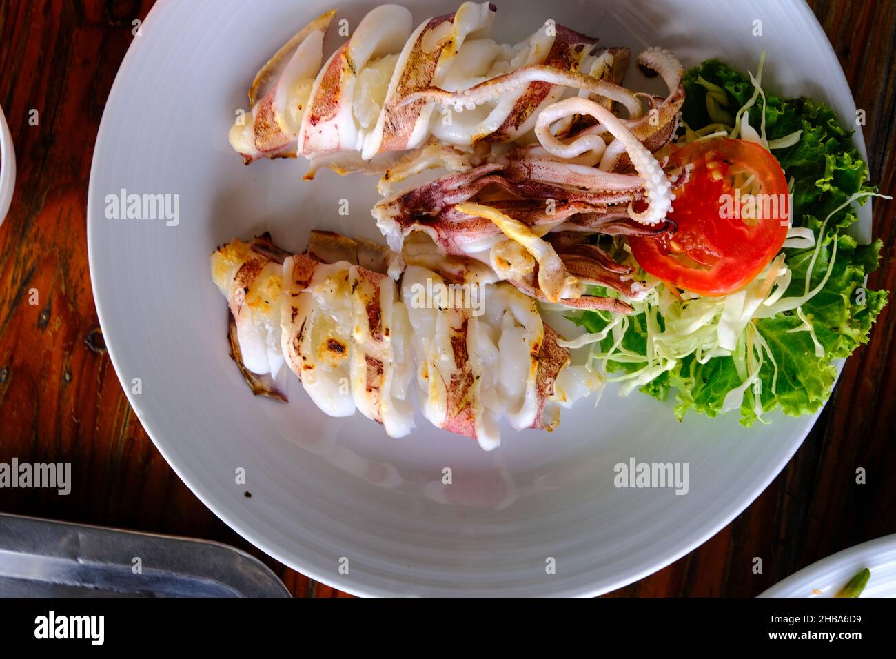 Grilled big squid serve in white disk with vegetable on wood table ...