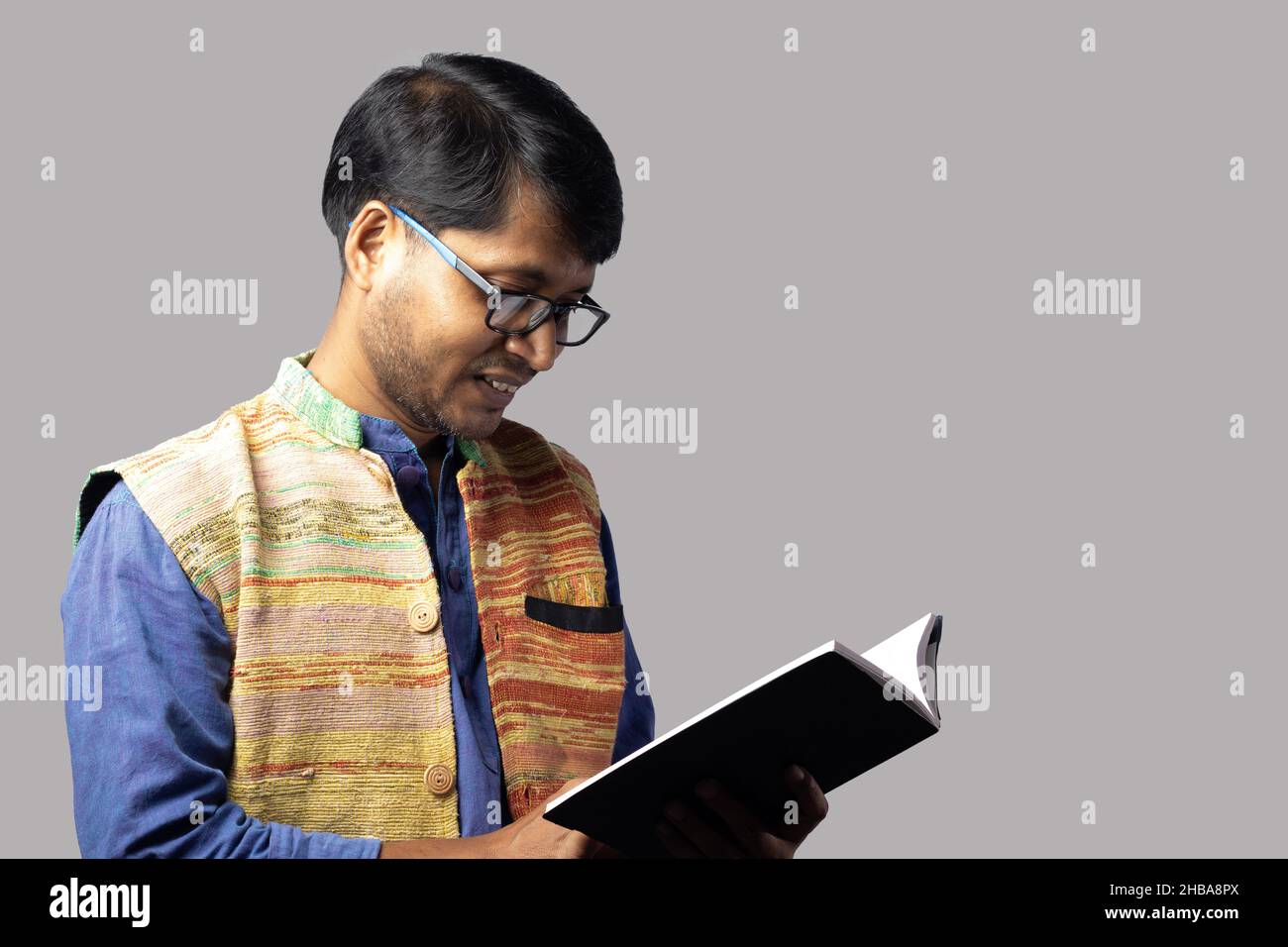 A young Indian male in ethnic dress reading book on gray background ...