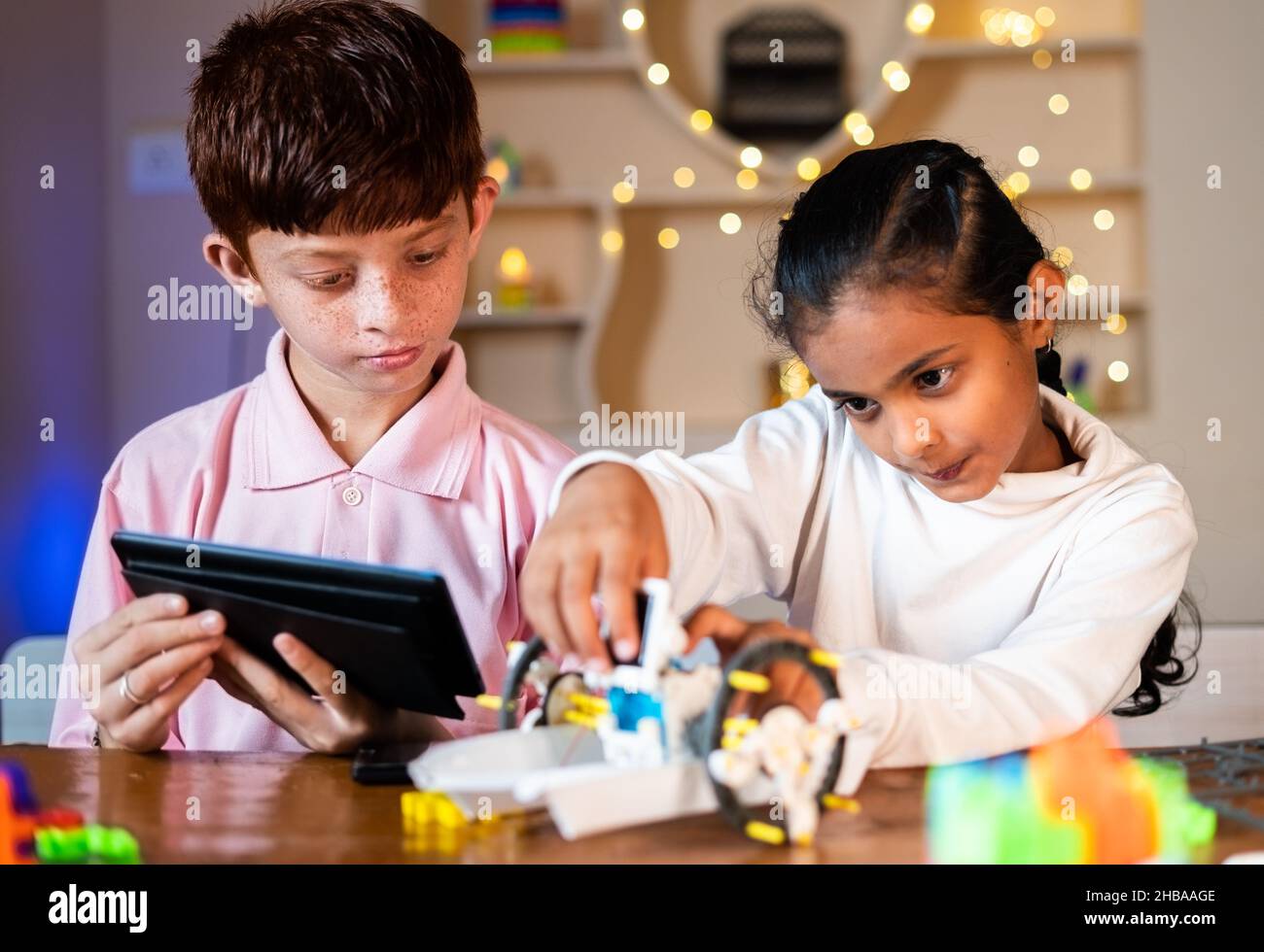 Kids busy making DIY robot by looking from digital tablet at home ...