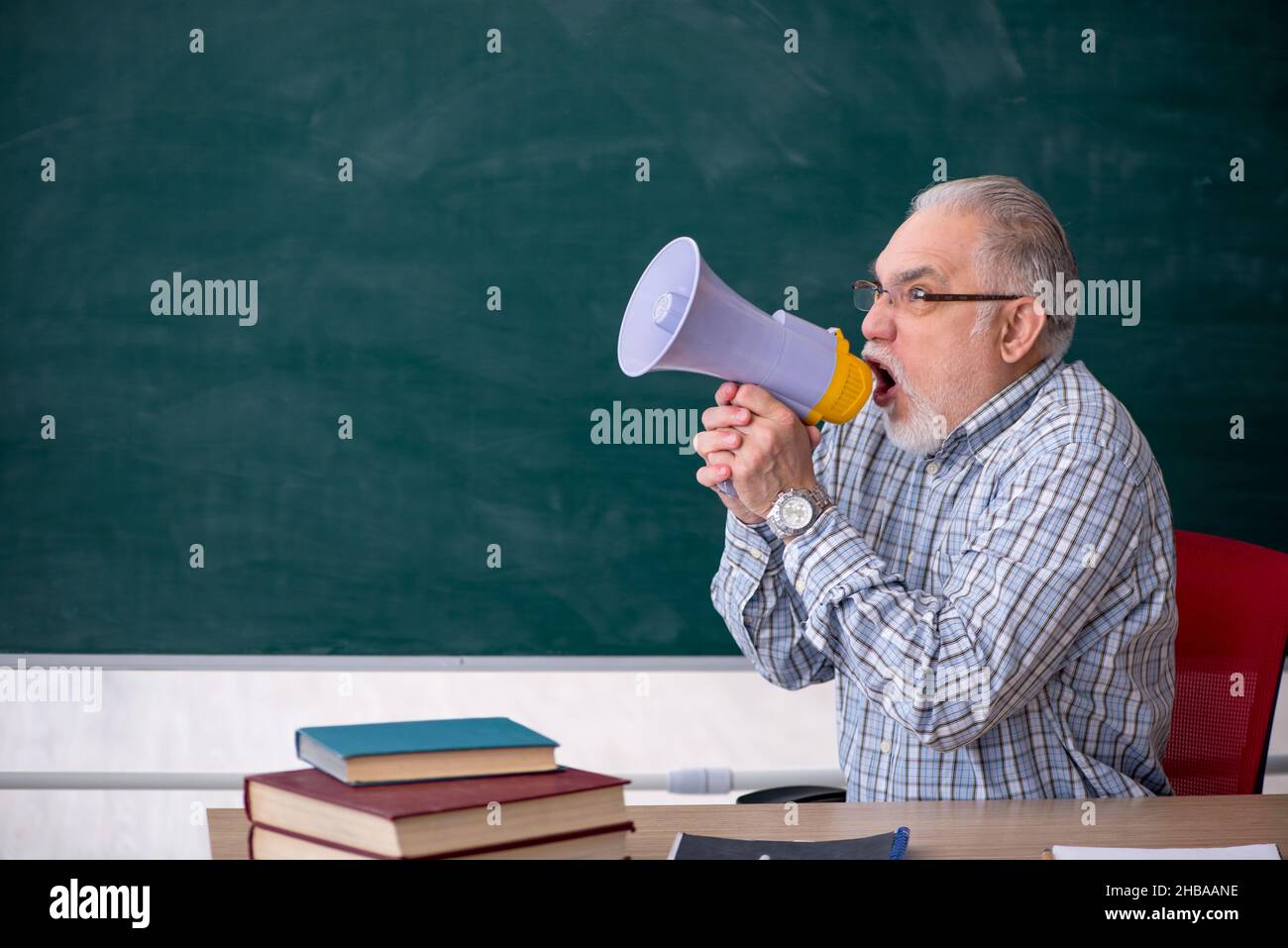 Aged male teacher holding megaphone in the classroom Stock Photo - Alamy