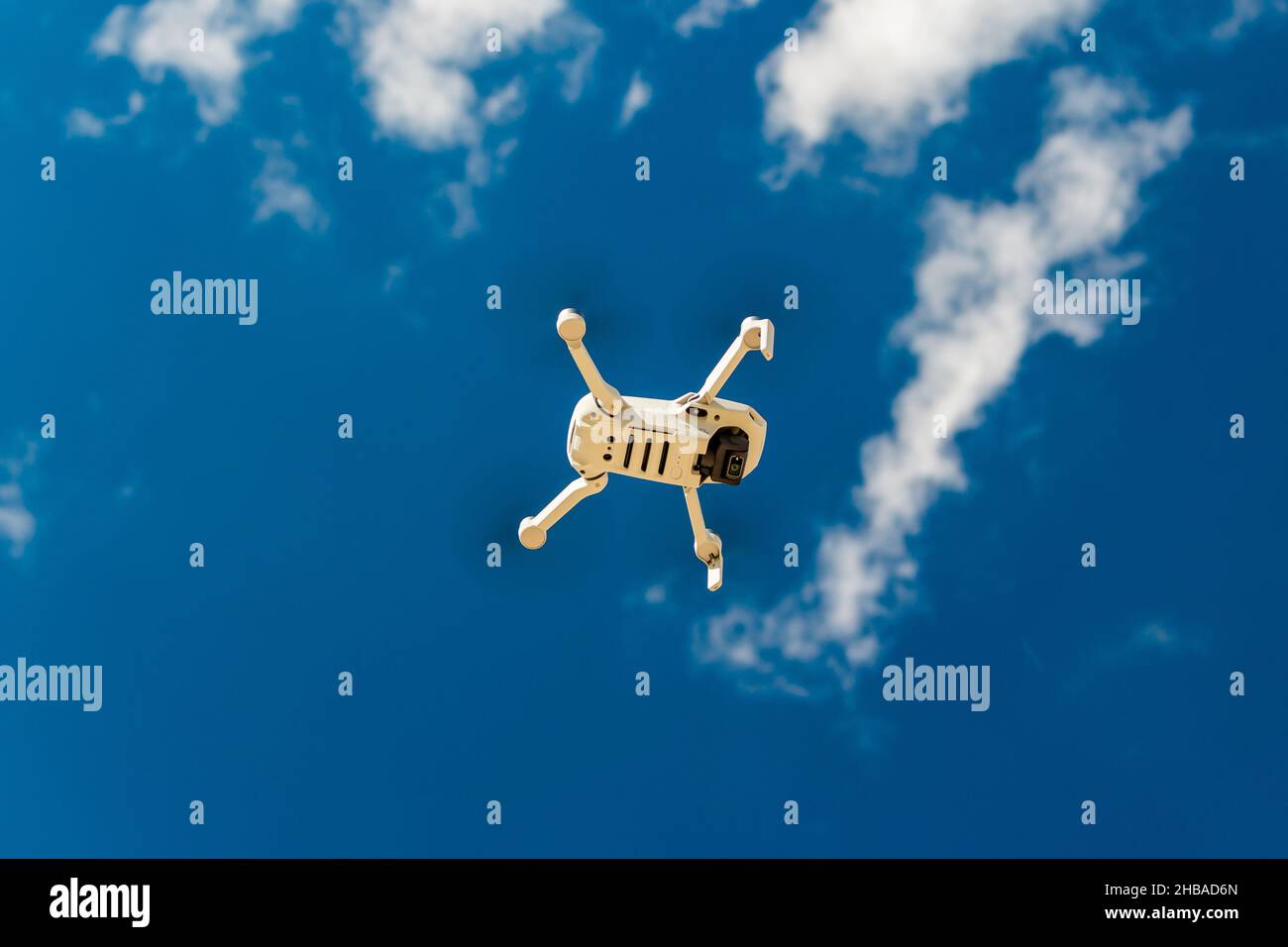 Small white drone DJI Mini 2 in flight against blue sky, bottom view ...