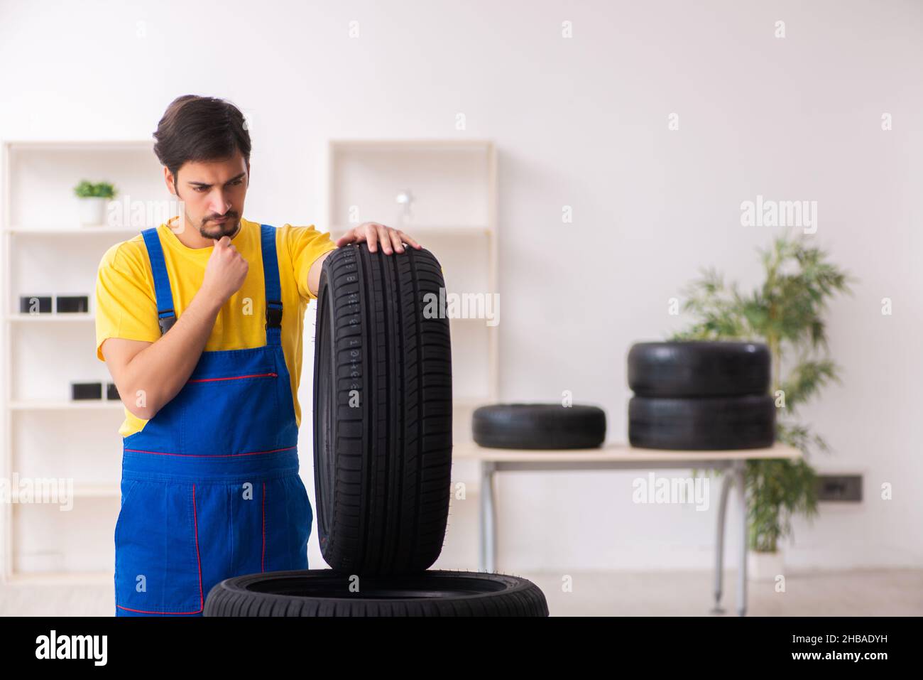 Young garage worker with tyre at workshop Stock Photo - Alamy