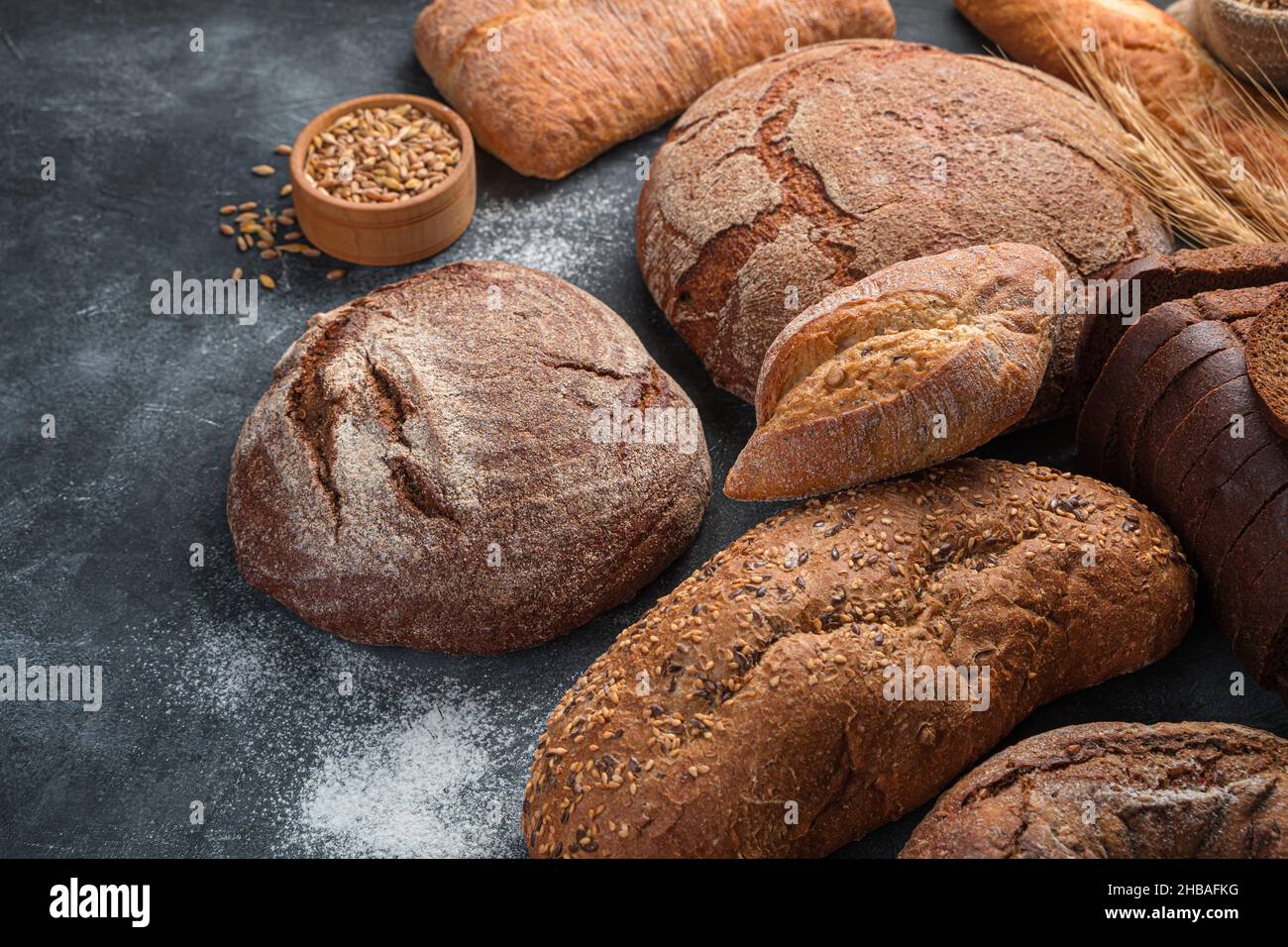 Different types of bread and wheat grains on a dark background. Side ...