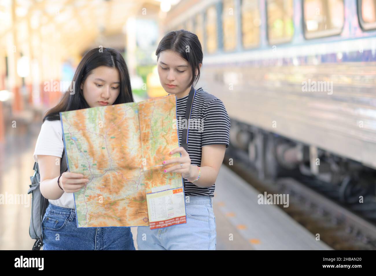 Two teenage girls looking at a map to travel by train, planning a train ...
