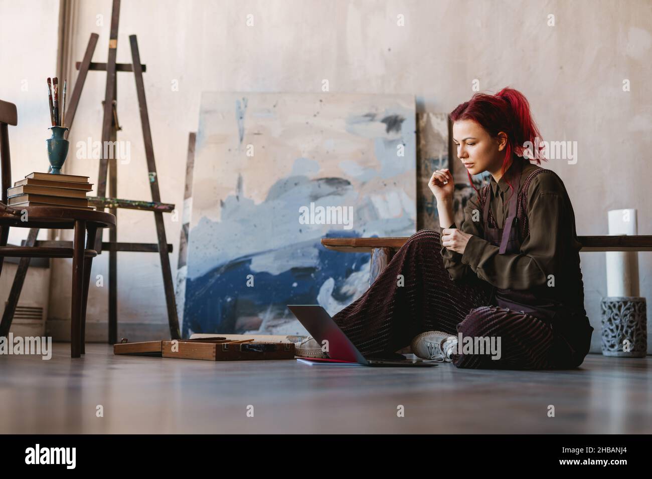 Young white woman painter in an art studio, using laptop computer for ...