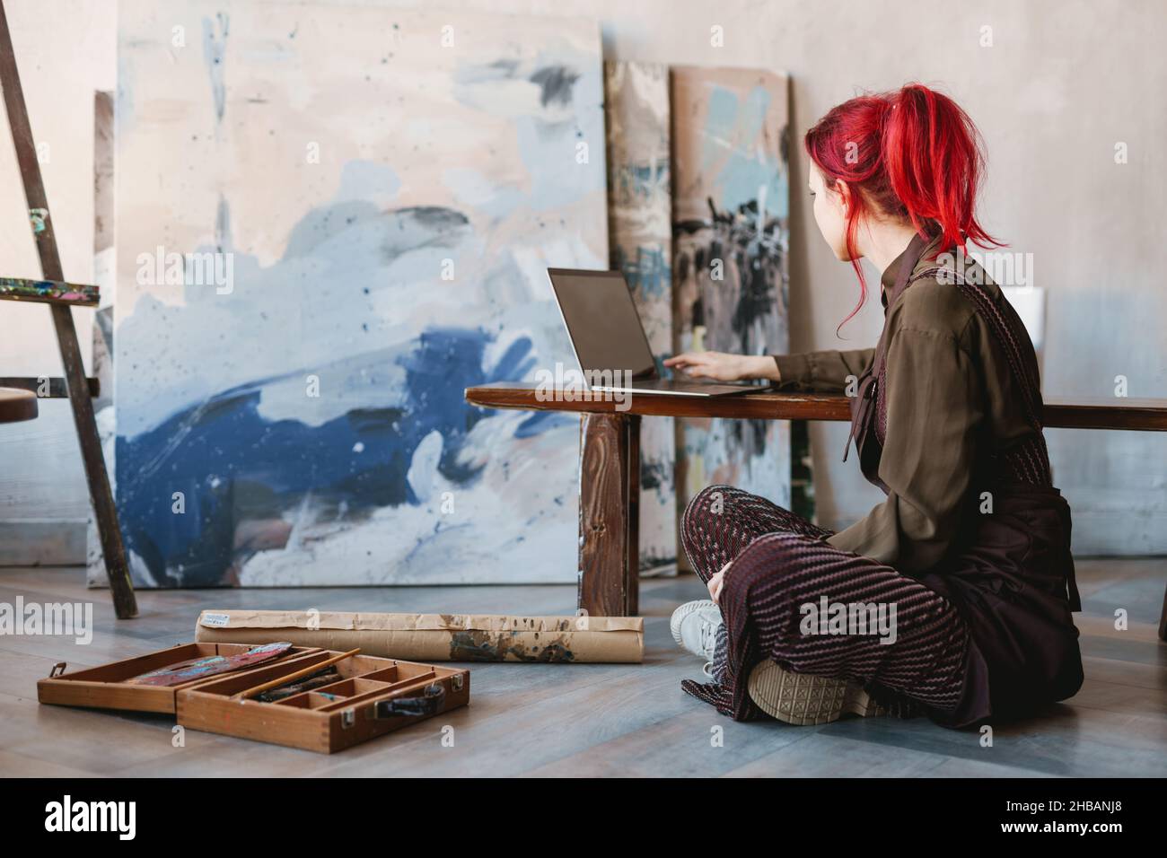 Young white woman painter in an art studio, using laptop computer for ...